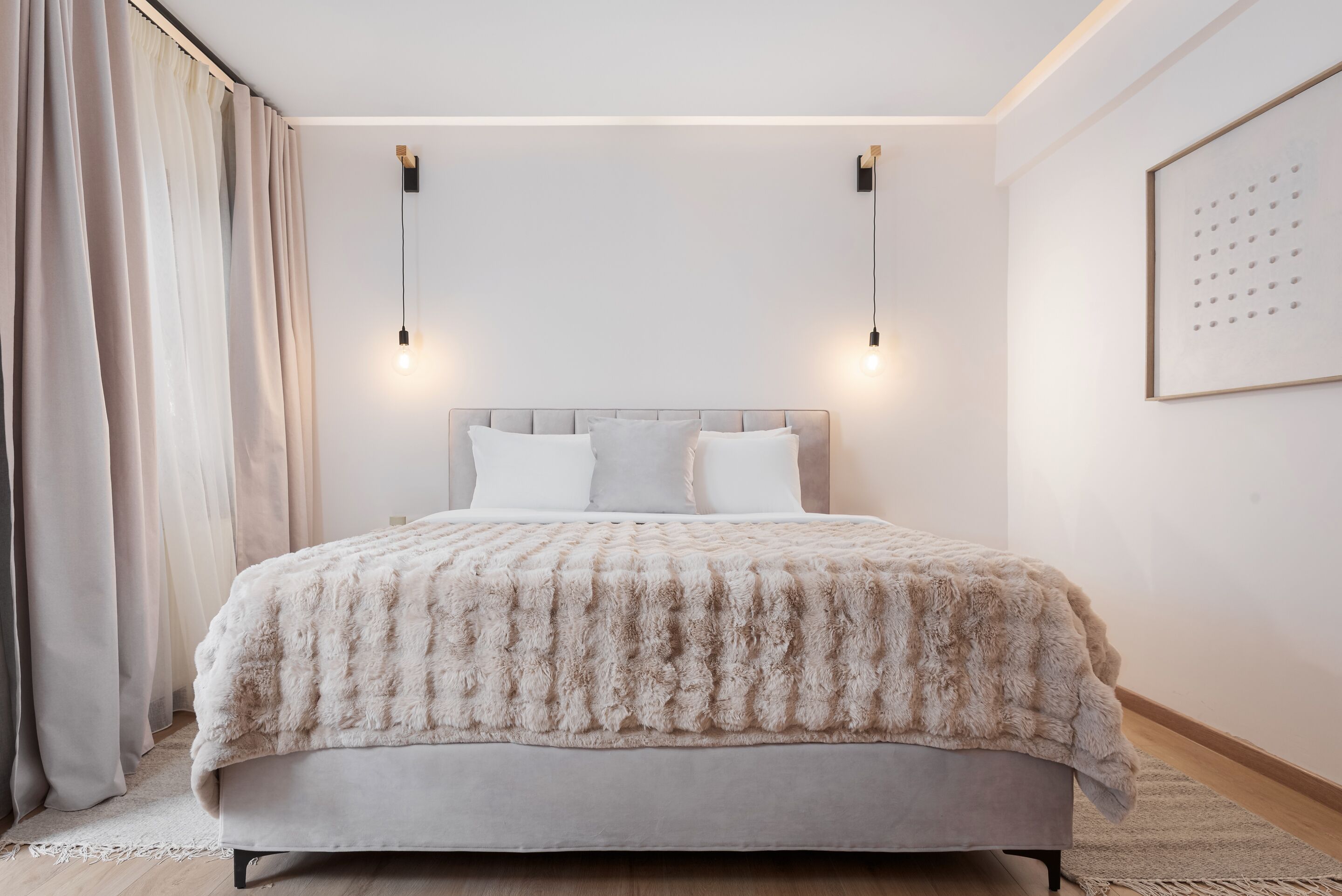 Quarto moderno com uma cama grande, duas luminárias de cabeceira e uma obra de arte emoldurada na parede.