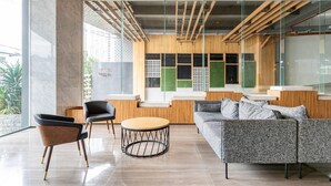 Um espaço de escritório moderno com teto de madeira, divisórias de vidro, um sofá cinzento e uma mesa redonda.