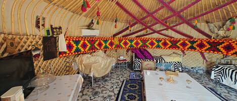 Um quarto em estilo de tenda com um painel de parede estampado, uma cama com colcha estampada, uma mesa com toalha branca e uma cadeira.