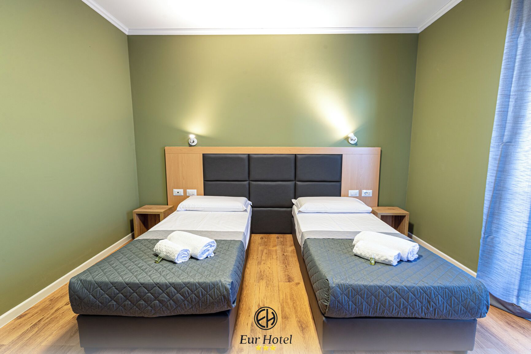 Quarto duplo com duas camas, cabeceiras de madeira e mesas de cabeceira com luminárias.