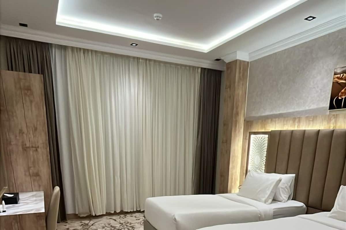 Quarto de hotel com duas camas, uma escrivaninha e uma cadeira.