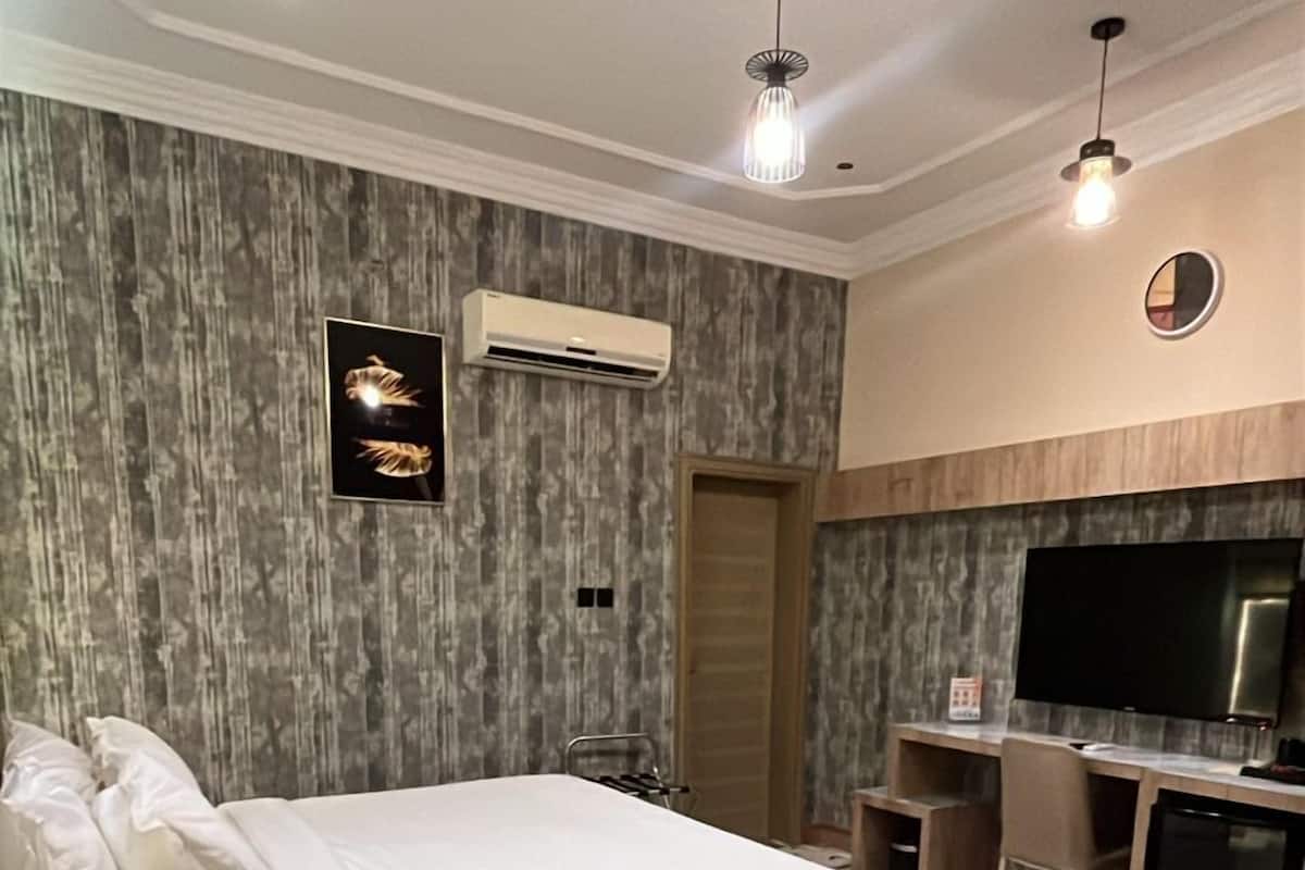 Quarto de hotel com cama, escrivaninha, televisão e ar condicionado.