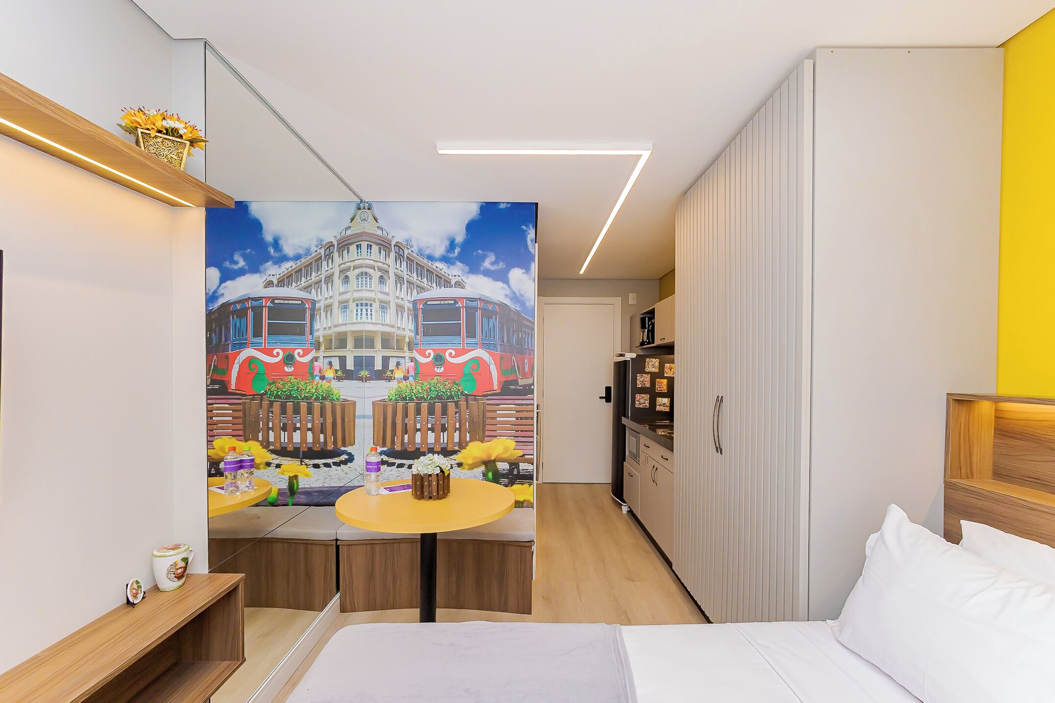 Quarto de hotel com uma cama, uma mesa pequena e um quadro de um elétrico na parede.