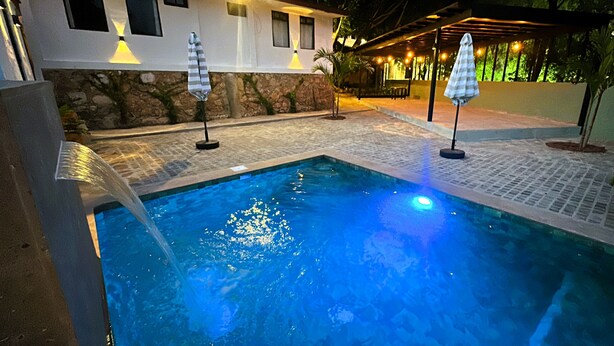 Piscina com muro de pedra e pergolado com iluminação.