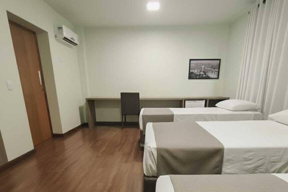 Quarto de hotel com duas camas, uma escrivaninha, uma cadeira e um quadro na parede.