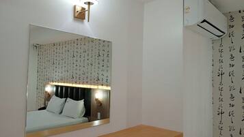 Quarto de hotel com cama, mesa de cabeceira, ar condicionado fixado na parede e decoração de parede com caligrafia.