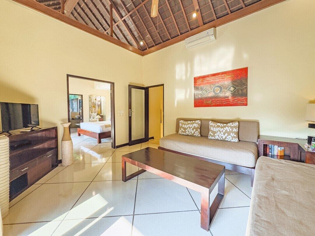 Uma sala de estar moderna com um sofá, mesa de centro e televisão. Há um quadro na parede e uma porta que dá para outro cômodo.