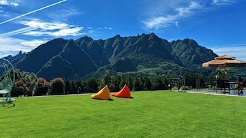 Uma área externa com gramado, dois sacos de feijão, uma cadeira de metal e uma estrutura com cobertura de palha.