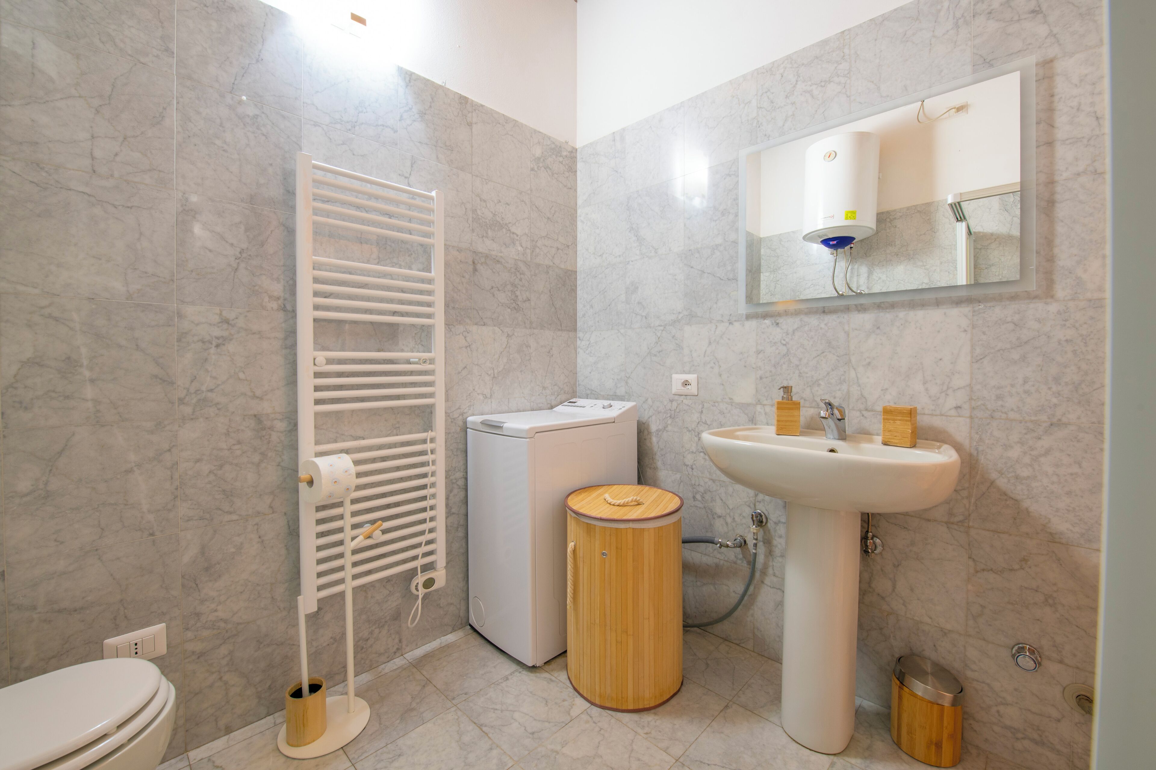 Uma casa de banho moderna com sanita, máquina de lavar roupa, lavatório e espelho.