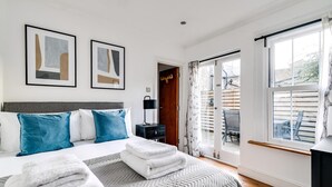 Um quarto com cama, almofadas, mesa de cabeceira e janela.