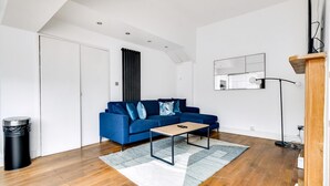 Uma sala de estar moderna com um sofá azul, uma mesa de centro de madeira e um espelho grande na parede.