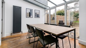 Quarto moderno com uma grande mesa de madeira, cadeiras pretas, um radiador e duas molduras na parede.