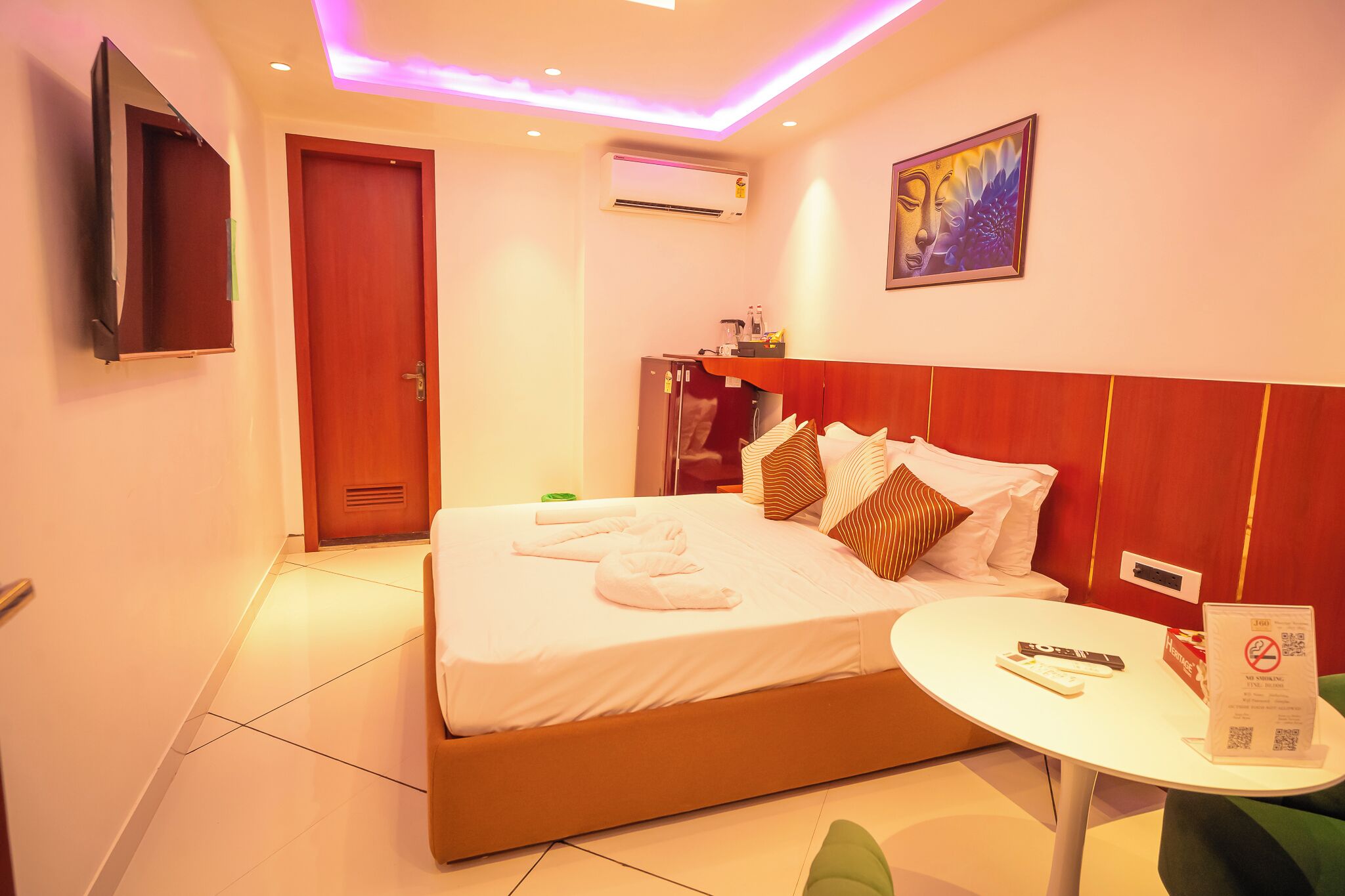 Quarto de hotel com cama, mesa de cabeceira, televisão na parede e um quadro sobre a cama.