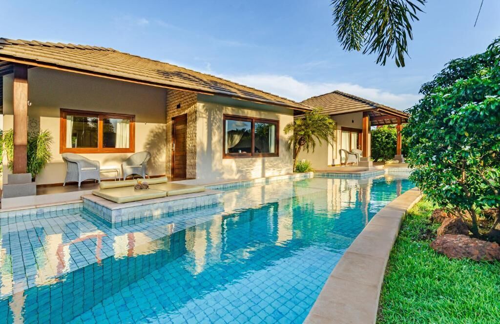 Uma área moderna na beira da piscina, com piscina transparente, duas espreguiçadeiras e um pérgola.