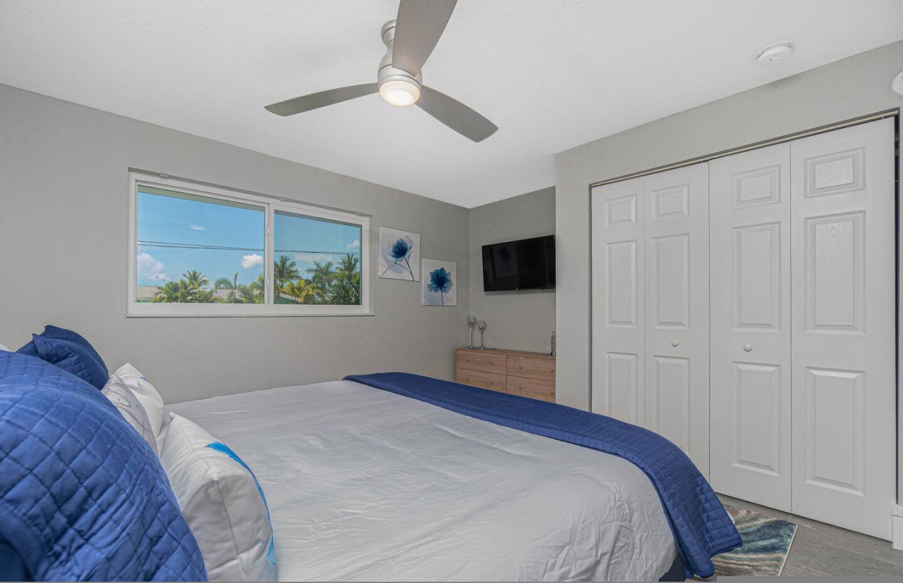 Quarto com cama, ventilador de teto, janela com vista, cômoda e televisão.