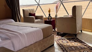 Quarto espaçoso com uma cama grande, duas poltronas e vista para uma paisagem desértica através de uma estrutura de janela geométrica.
