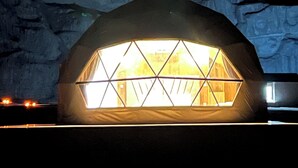 Uma tenda em formato de abóbada com design de janela triangular, montada diante de um cenário de rochas.