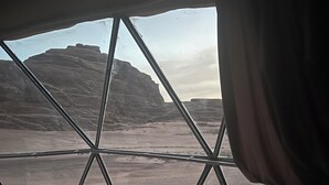 Quarto com uma grande janela que oferece vista para uma paisagem desértica com formações rochosas.