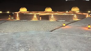 Um edifício grande e iluminado com várias estruturas em cúpula, situado contra um cenário montanhoso.