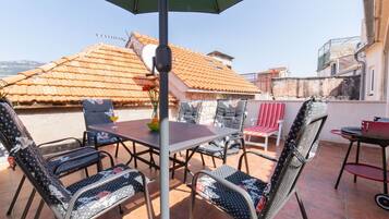 Um pátio com mesa, cadeiras, churrasqueira e vista para edifícios com telhados de terracota.