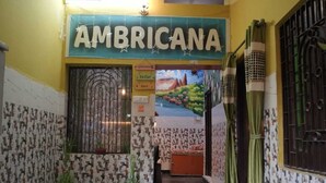Entrada de um hotel com uma placa indicando "AMBRICANA", uma escadaria e um mural na parede.
