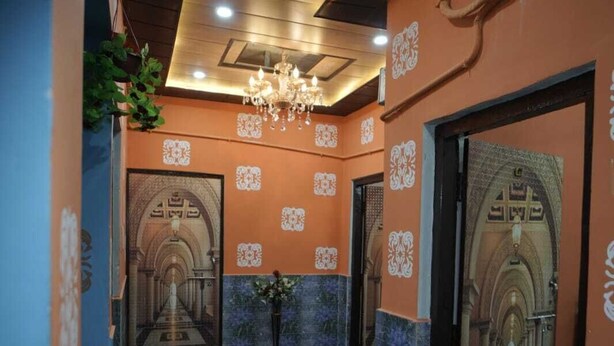 Um corredor com designs ornamentais nas paredes, um candelabro e um tapete vermelho que leva a uma porta com um arco decorativo.