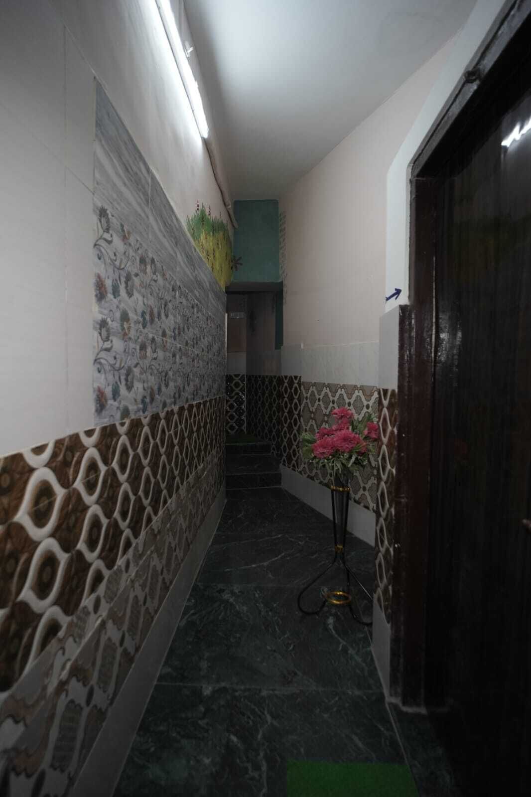 Um corredor estreito com paredes estampadas, chão de mármore e uma porta à direita.