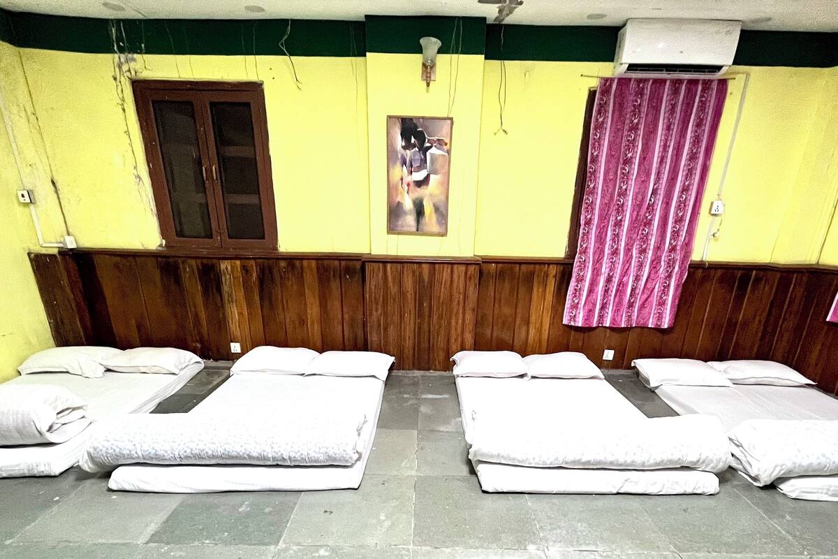 Quarto com quatro camas alinhadas, painéis de madeira nas paredes, uma janela e um ar condicionado fixado na parede.