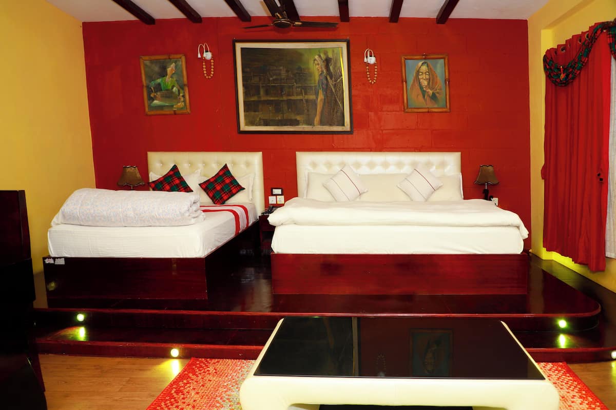 Quarto de hotel com duas camas, uma mesa de centro de vidro e uma cortina vermelha.