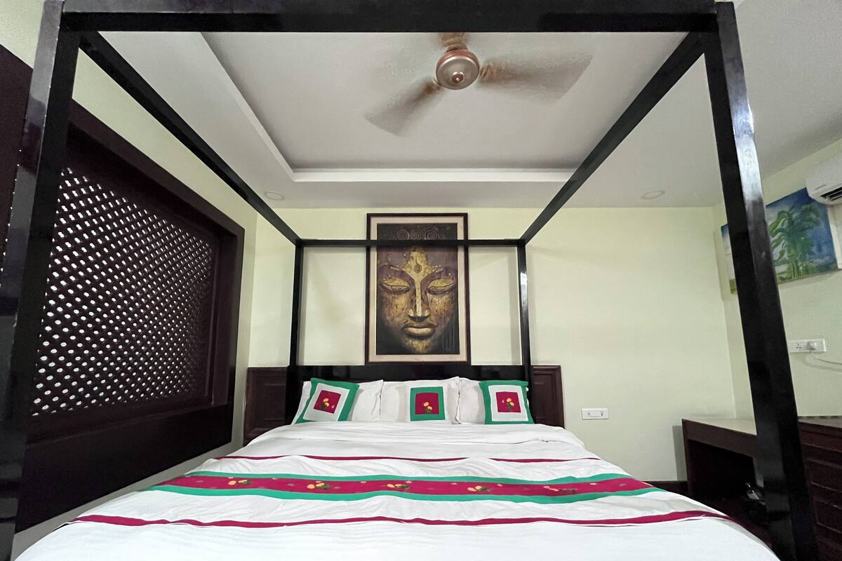 Uma cama de dossel com um ventilador de teto, uma pintura de Buda e um painel decorativo na parede.