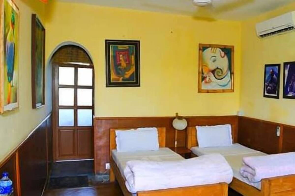 Quarto com duas camas, cabeceira de madeira, uma porta e várias pinturas nas paredes.