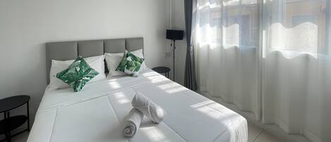 Quarto de hotel com cama, mesa de cabeceira, abajur e janela com cortinas.