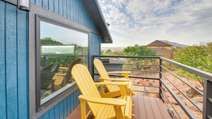 Uma varanda com cadeiras Adirondack, uma porta de vidro e vista para uma paisagem montanhosa.