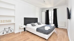 Quarto moderno com uma cama grande, uma mesinha de cabeceira, uma bicicleta e vista para o exterior.