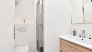 Casa de banho moderna com sanita branca, cabine de duche em vidro, espelho e lavatório com móvel de madeira.