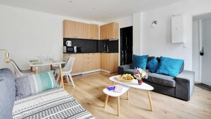 Uma sala de estar moderna com um sofá cinza, uma mesa de centro e uma área de refeições com uma mesa e cadeiras brancas.