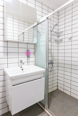 Um banheiro com pia branca, box de vidro e parede revestida com azulejos.