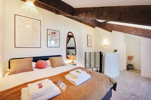 Quarto de hotel com cama, viga de madeira no teto, espelho e obras de arte emolduradas na parede.