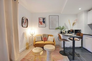 Uma sala de estar moderna com sofá, mesa de centro, área de jantar com cadeiras e cozinha ao fundo.