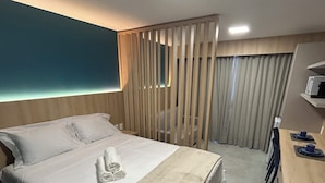 Quarto de hotel com cama, escrivaninha e janela com cortinas.