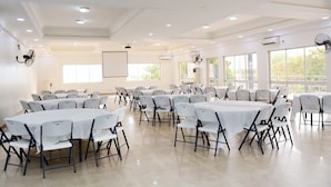 Uma sala de conferência com várias mesas e cadeiras, janelas amplas, ventiladores de teto e uma tela de projetor.