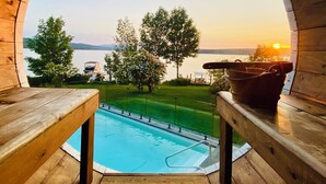 Um deck de madeira com piscina e vista para um lago e árvores ao pôr do sol.