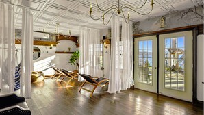 Um quarto amplo com piso de madeira, um lustre grande e vista através de uma porta de vidro.