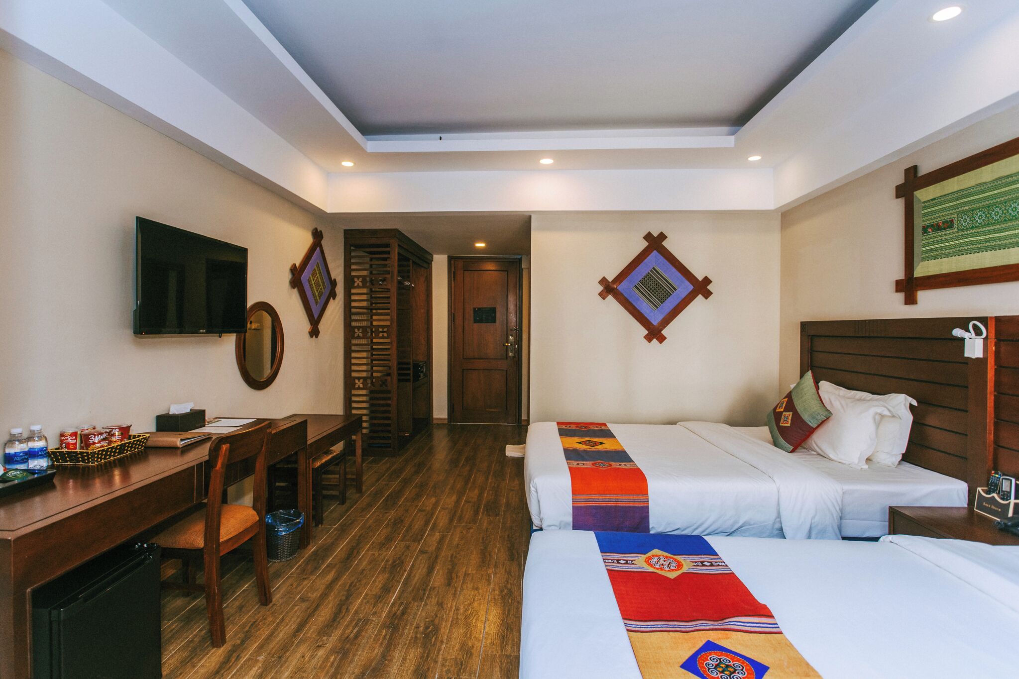 Quarto de hotel com duas camas, uma escrivaninha, televisão e uma porta que dá para outro aposento.