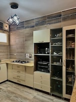 Cozinha moderna com fogão a gás, forno embutido e micro-ondas. Há um armário com portas de vidro exibindo utensílios de cozinha.