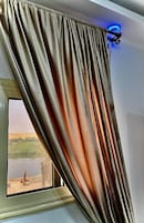 Janela com vista para paisagem, cortinas entreabertas e luminária azul na parede.