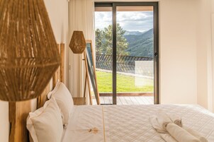 Quarto com uma cama grande, vista para uma varanda com deck de madeira e paisagem montanhosa.
