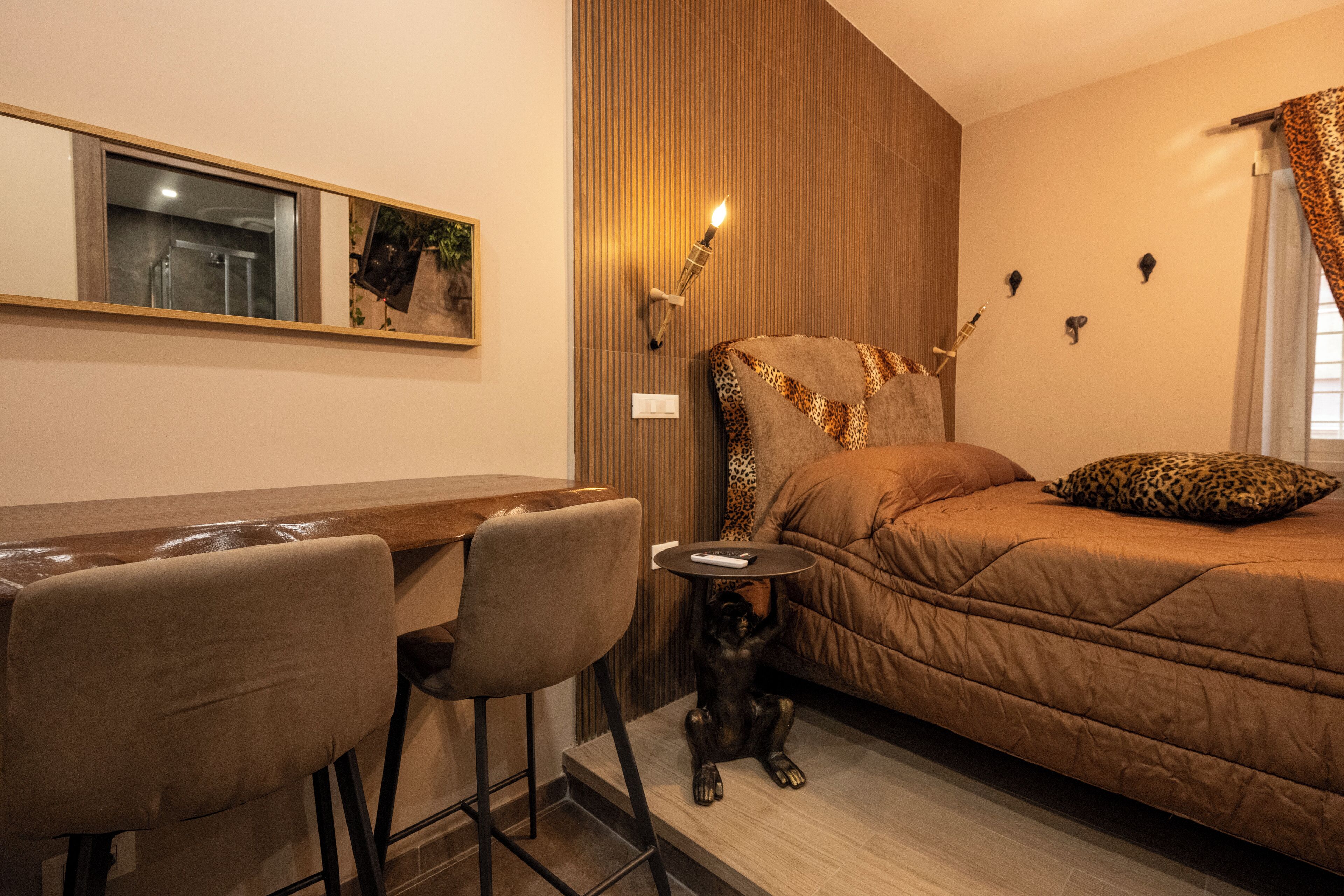 Quarto com cama, escrivaninha, duas cadeiras, mesa pequena e mesa de cabeceira.
