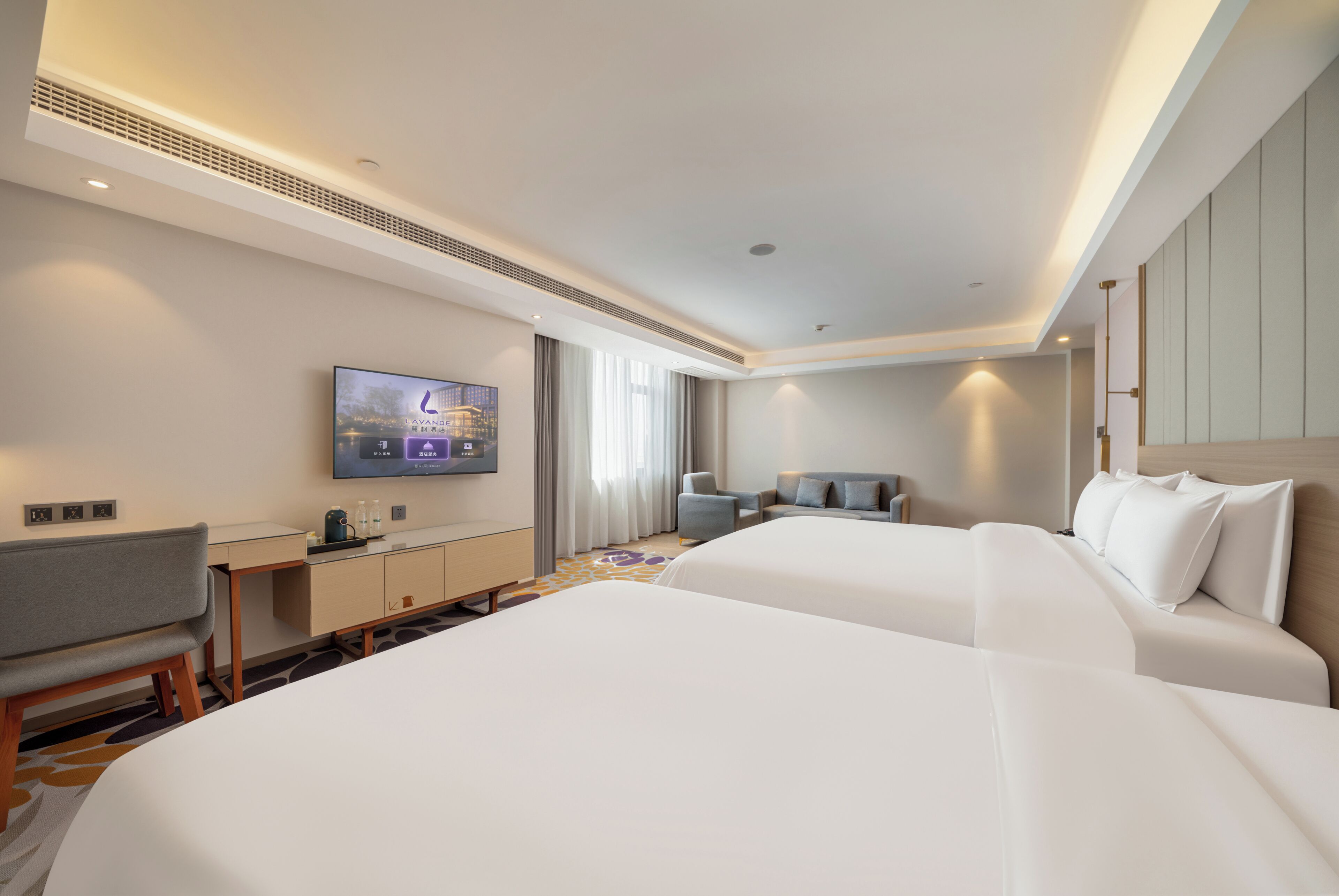 Quarto de hotel com duas camas, uma escrivaninha, uma cadeira, uma televisão e uma janela grande.