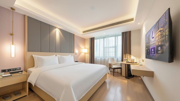 Quarto de hotel moderno com uma cama grande, mesa de cabeceira, luminária, televisão e uma escrivaninha com cadeira.